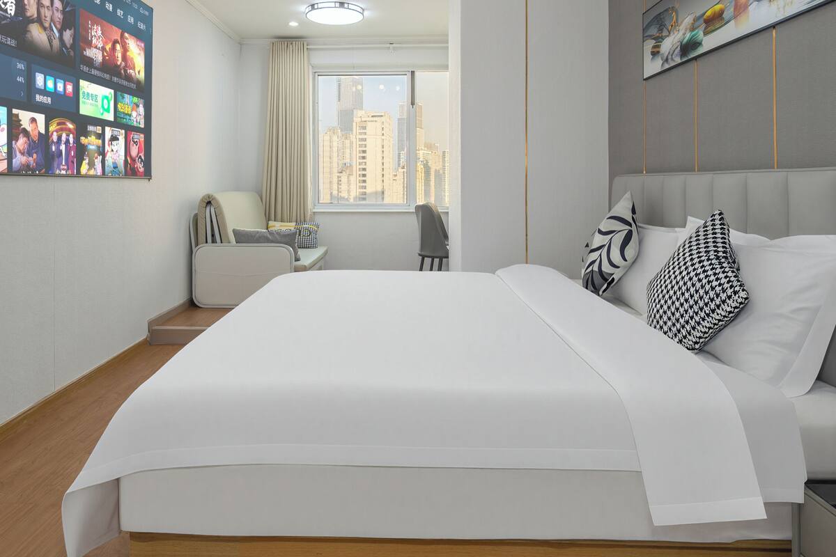 Quarto de hotel moderno com uma cama grande, ventilador de teto, TV fixada na parede e janela com vista para a cidade.