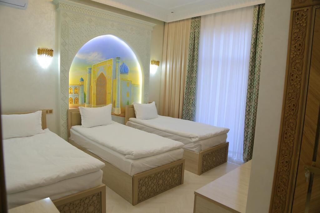 Quarto de hotel com duas camas de solteiro, uma mesinha e um arco decorativo com um mural.