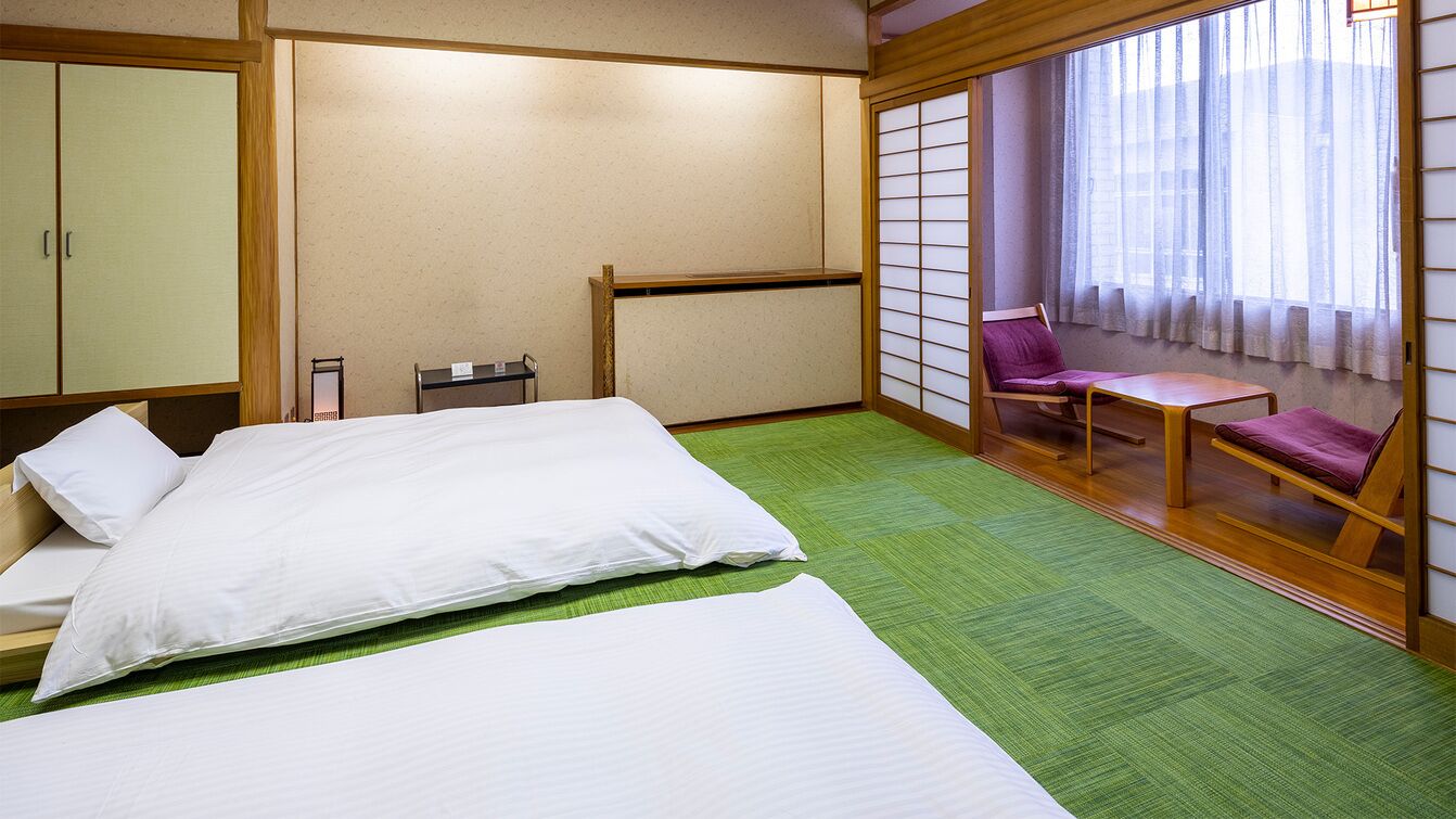 Quarto de hotel com cama, escrivaninha, cadeira e vista através de um ecrã shoji.