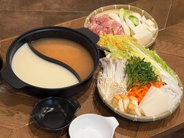 Um conjunto de panela com diversos ingredientes, como vegetais, tofu e carne, além de uma tigela de sopa.
