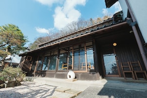 Um edifício japonês tradicional com telhado de telhas, janelas amplas e um candeeiro de pedra na entrada.