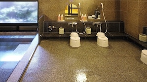 Sala de sauna com um espelho grande, vários chuveiros e uma tela de televisão.