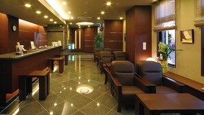 Um saguão de hotel com balcão de recepção, área de estar e uma luminária circular grande no teto.
