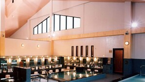Uma grande piscina interior com várias pistas de natação, uma área de relaxamento separada e um teto alto com claraboias.