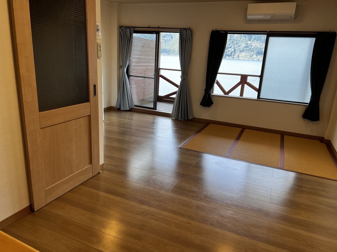 Quarto com piso de madeira, porta de correr de vidro e vista para um deck de madeira e água.