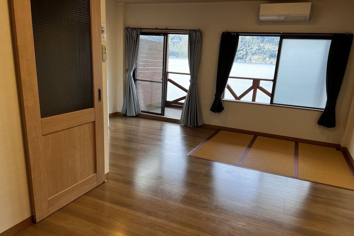 Quarto com piso de madeira, porta de correr de vidro e vista para um deck de madeira e água.