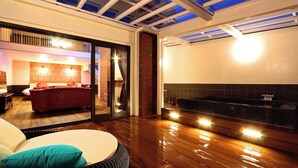 Uma área de spa moderna com um sofá vermelho, uma banheira grande e uma porta de vidro que dá para um quarto.