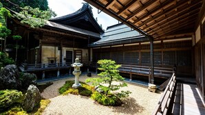 Um edifício tradicional japonês com estrutura de madeira, um candeeiro de pedra e uma pequena árvore na área do jardim.