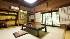 Um espaço com tatames, uma mesa baixa, um assento e uma porta tradicional japonesa deslizante, com vista para o exterior.