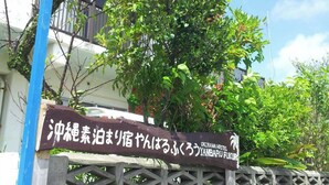 Placa com texto em japonês e o nome 'OKINAWA HOSTEL' indicando uma hospedaria.