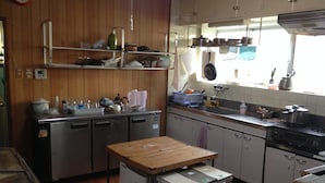 Uma cozinha com armários de madeira, uma geladeira de aço inoxidável, uma mesa de madeira e uma lixeira com etiquetas de reciclagem.