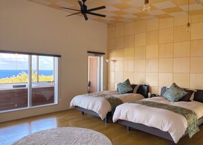 Quarto com duas camas, ventoinha no teto, janela grande com vista para o mar e abajur.