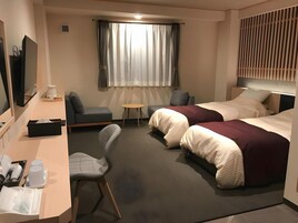 Quarto de hotel com duas camas, uma escrivaninha com cadeira, uma mesinha e uma televisão.