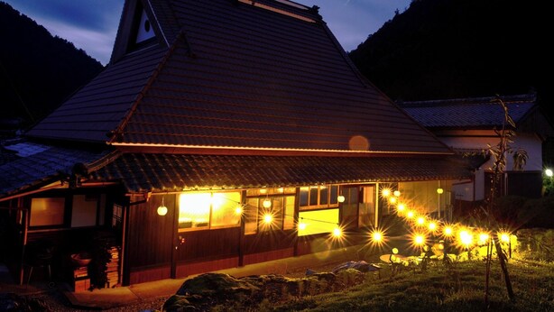 Uma casa tradicional japonesa com telhado inclinado, fachada de madeira e uma série de luzes na frente.