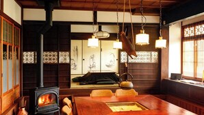 Quarto em estilo japonês tradicional, com mesa de jantar de madeira, cadeiras, lareira e portas corrediças com arte.