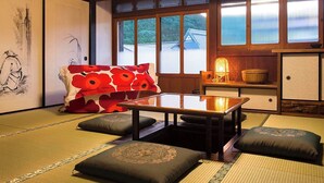 Um quarto japonês tradicional com tatames, uma mesa baixa, almofadas e vista para uma paisagem nevada através de grandes janelas.