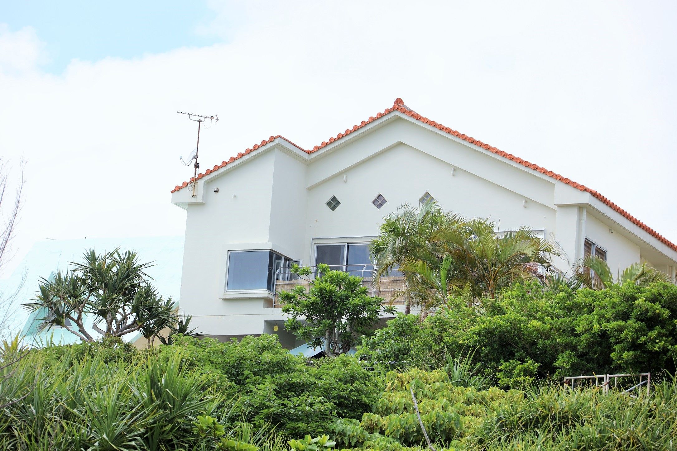 Um edifício de dois andares com telhado de telhas vermelhas, antena parabólica e varanda.