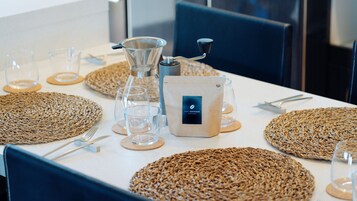 Mesa posta com utensílios para café, copos e jogos americanos trançados.