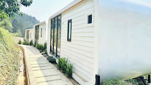 Fileira de cabanas modernas, brancas e térreas, com grandes janelas e um caminho que as leva até elas.