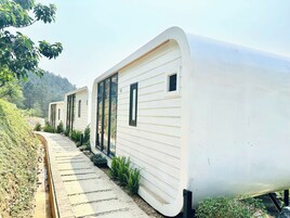 Fileira de cabanas modernas, brancas e térreas, com grandes janelas e um caminho que as leva até elas.