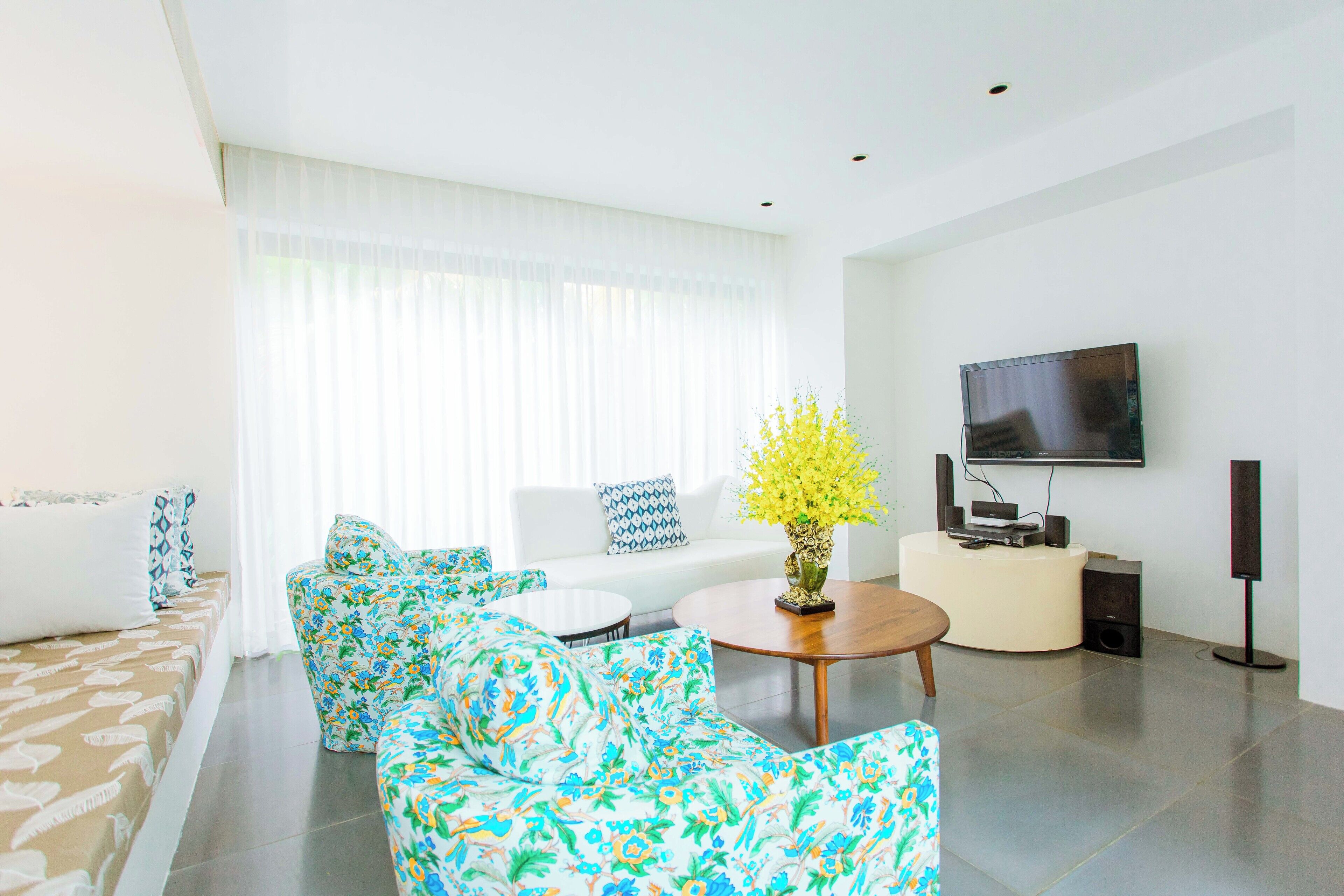 Uma sala de estar moderna com sofá, poltronas, mesa de centro, TV e um alto-falante.