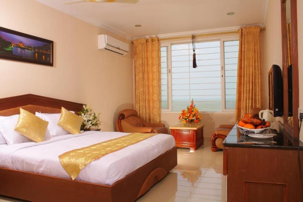 Quarto de hotel com uma cama grande, uma escrivaninha com computador, uma cadeira e uma janela com cortinas.