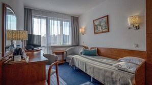 Quarto de hotel com cama, secretária com televisão, cadeira, abajur e janela com cortinas.