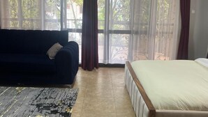 Quarto com cama, sofá e uma janela grande com cortinas.