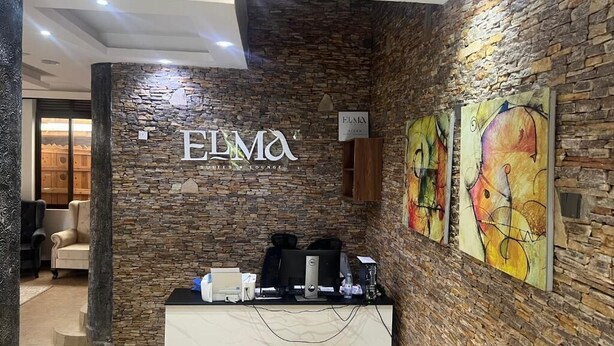 Uma área de recepção com parede de pedra, um balcão com computador e obras de arte na parede.