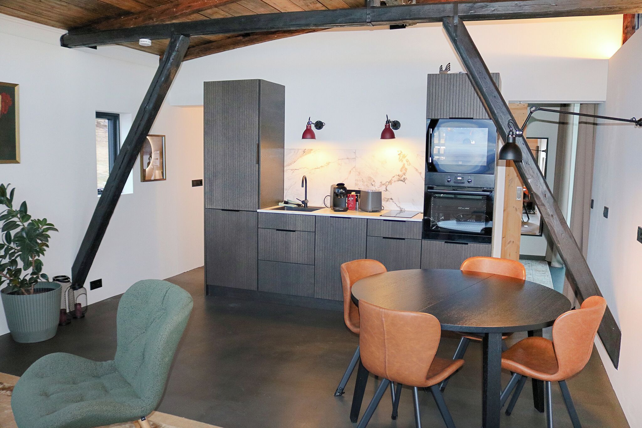 Cozinha moderna com forno embutido, máquina de café e televisão. Possui área de jantar com mesa redonda e quatro cadeiras.