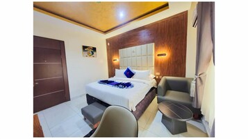 Quarto de hotel com cama, escrivaninha, cadeira e mesa pequena.