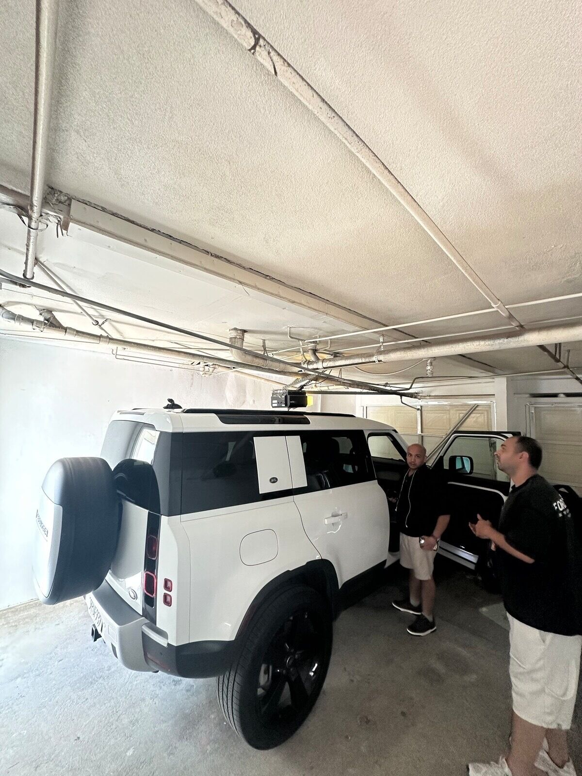 Um SUV branco estacionado em uma garagem com canos no teto e piso de concreto.