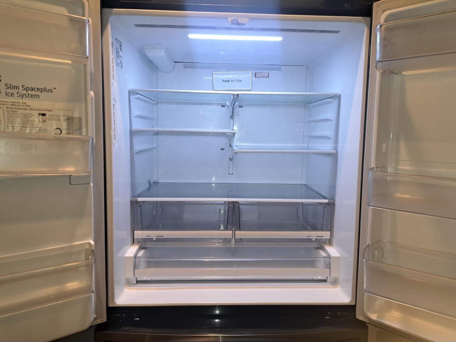 Uma geladeira vazia com prateleiras identificadas para frutas e vegetais, um filtro de ar renovado e um dispensador de água.