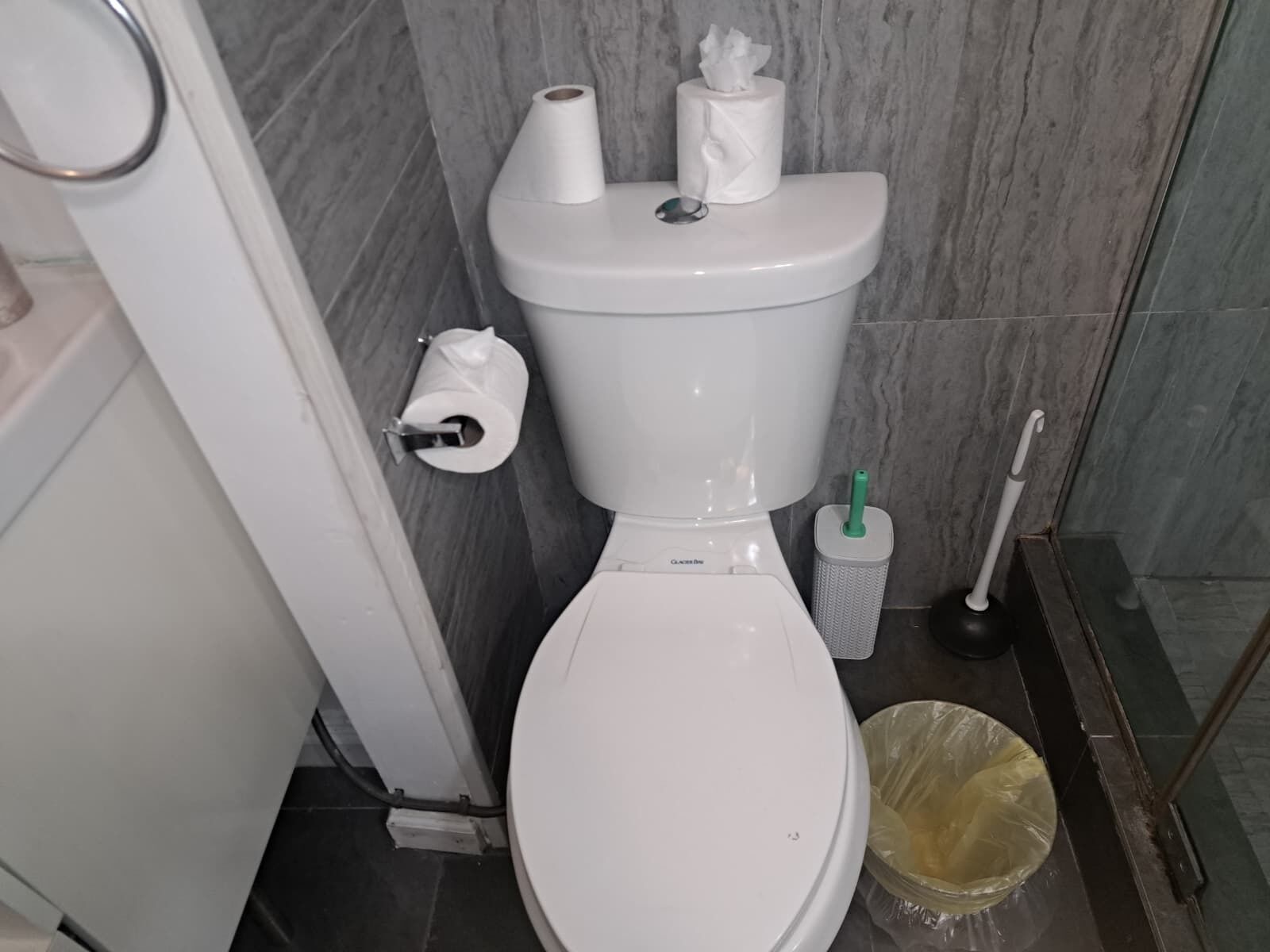 Casa de banho com sanita, rolo de papel higiénico, bidé e um cesto de lixo.