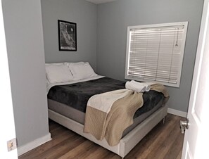 Quarto com cama, janela com persianas, mapa emoldurado na parede e porta.