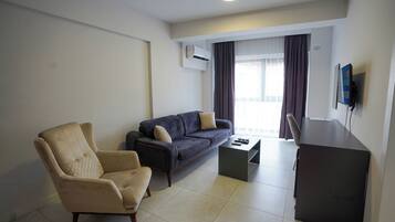 Uma sala de estar com sofá, poltrona, mesa de centro e televisão fixada na parede.