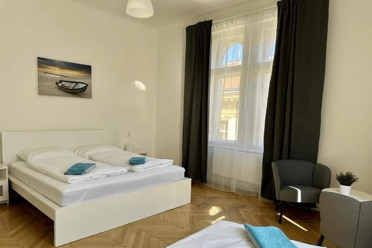 Quarto de hotel moderno com cama, poltrona, escrivaninha e janela com cortinas.
