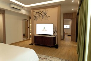 Quarto de hotel com cama, televisão sobre um suporte de madeira, espelho e televisão fixada na parede.