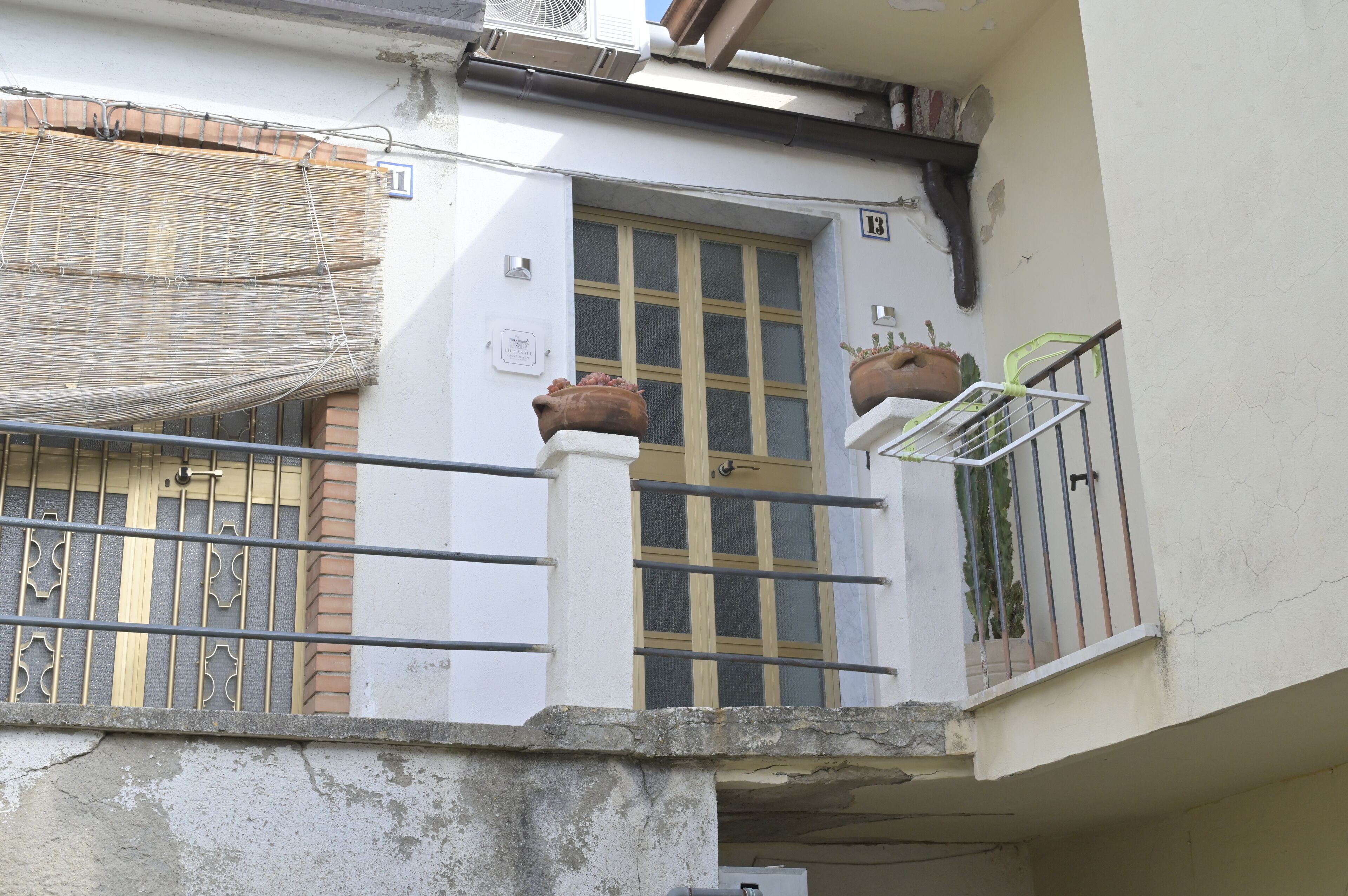 Um edifício com fachada branca, uma janela com moldura amarela e uma varanda com grade de metal.