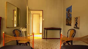 Um quarto com duas cadeiras de vime, uma mesinha, um espelho e obras de arte nas paredes.