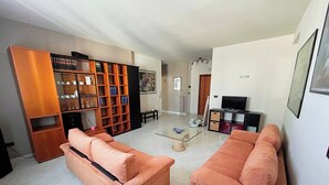 Uma sala de estar com dois sofás, uma mesa de centro, uma estante e uma televisão.