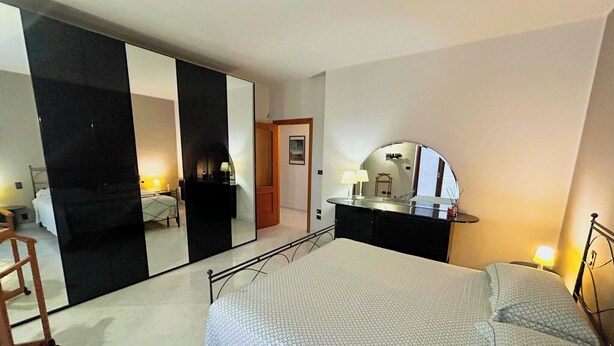 Quarto com uma cama grande, cômoda, espelho e guarda-roupa.
