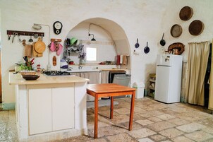 Cozinha com ilha central, fogão, pia e diversos utensílios pendurados na parede.