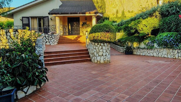 Uma casa de dois andares com entrada em azulejos, paredes de pedra e montanhas ao fundo.