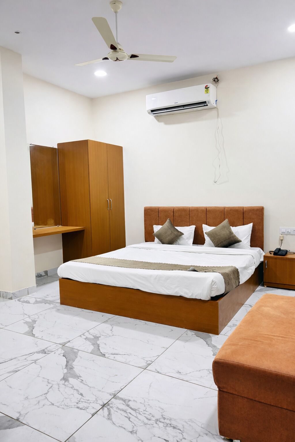 Quarto com cama, guarda-roupa, mesa de cabeceira, sofá, ventoinha de teto e ar condicionado.