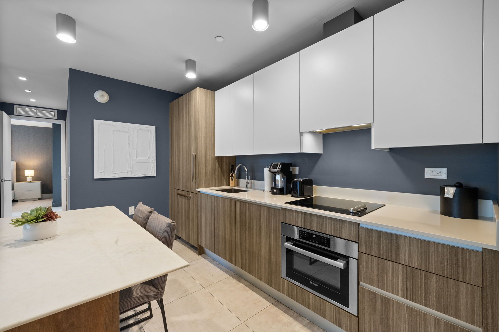 Uma cozinha moderna com uma ilha central, eletrodomésticos embutidos e uma parede de destaque azul-escuro.