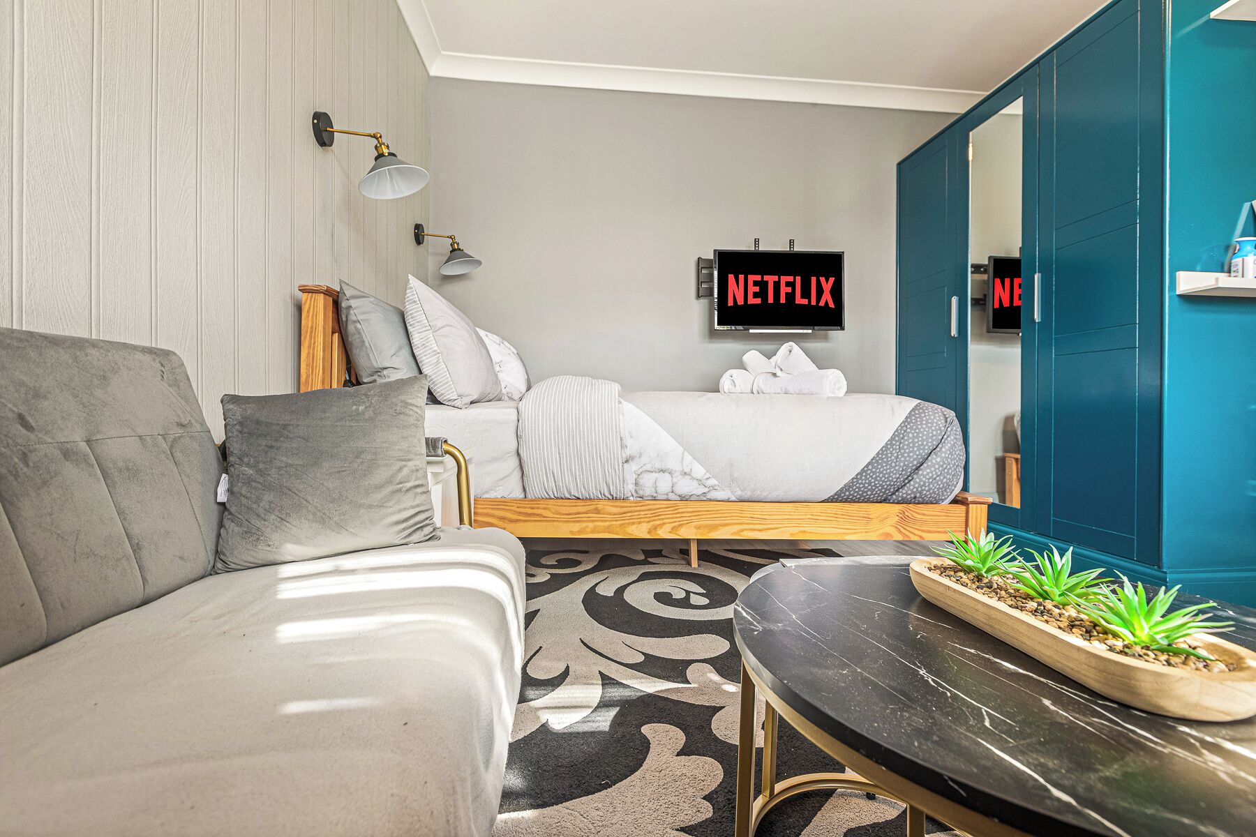 Quarto moderno com cama, sofá, TV exibindo 'NETFLIX' e armário.