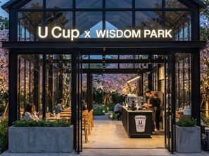 Fachada moderna da U Cup x Wisdom Park com estrutura de vidro, área externa com mesas e balcão de café.