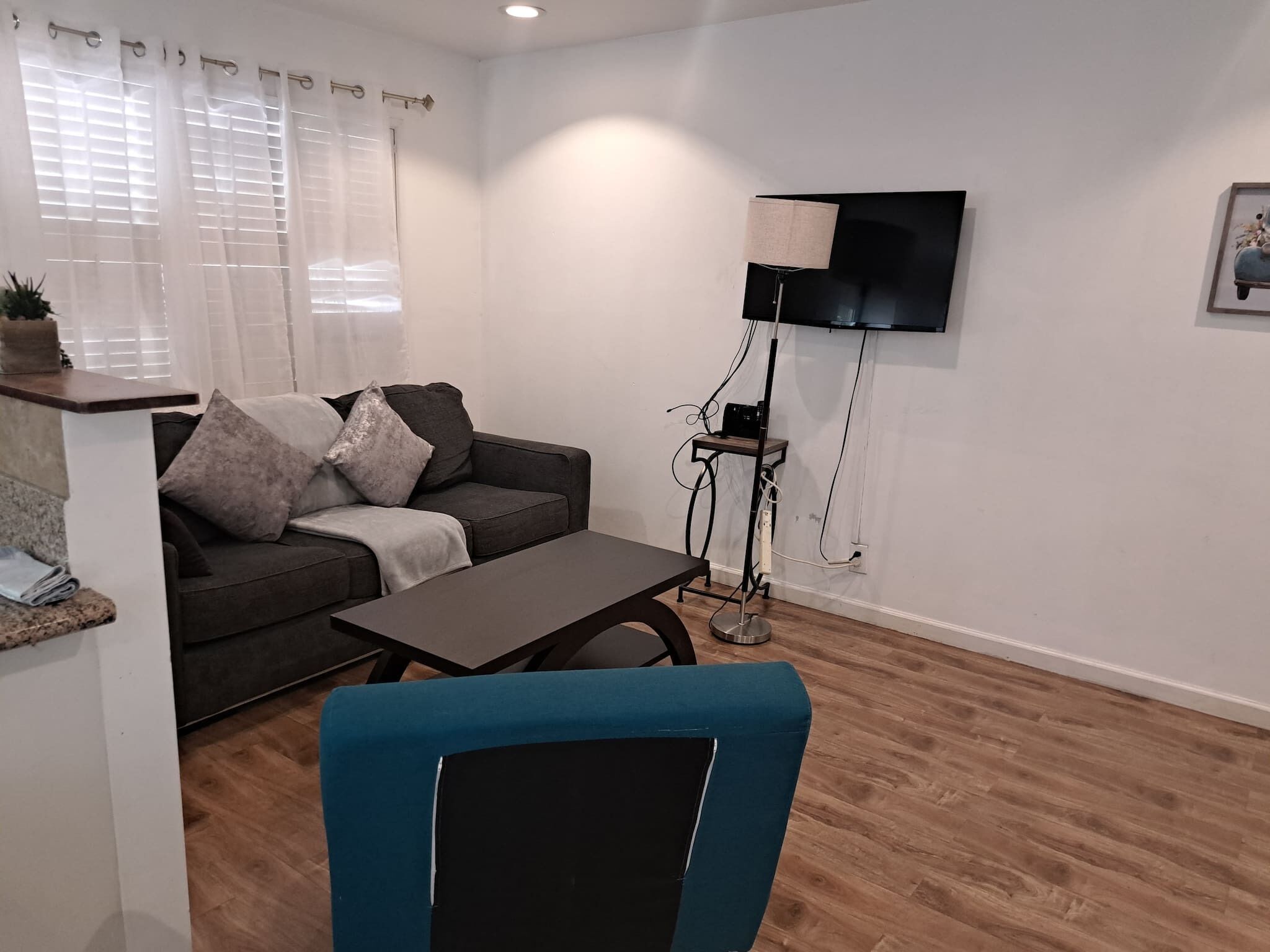 Uma sala de estar moderna com um sofá cinza, uma poltrona azul, uma mesa de centro e uma TV fixada na parede.