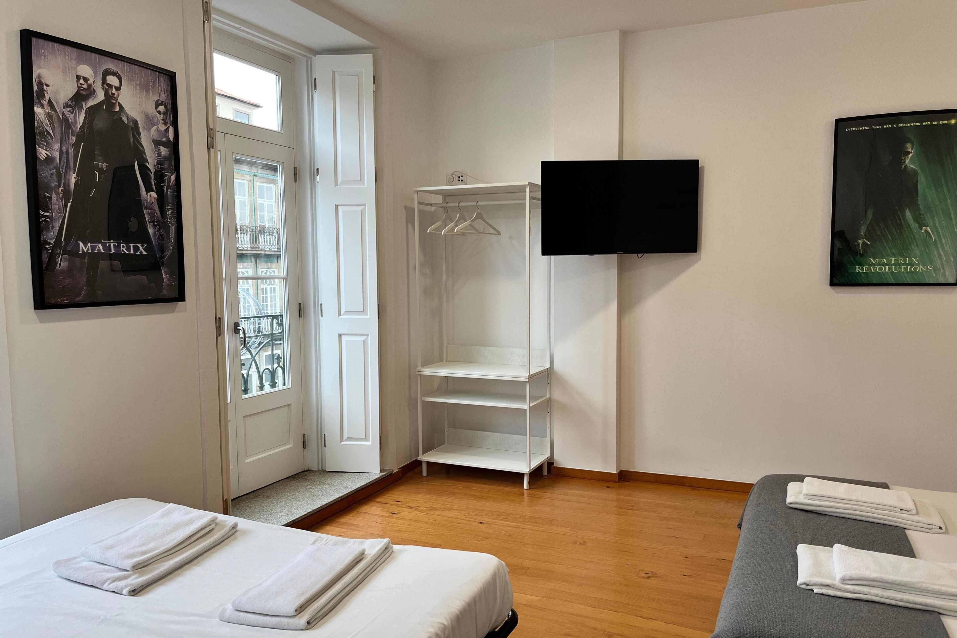 Quarto de hotel com cama, guarda-roupa, televisão e cartazes nas paredes.